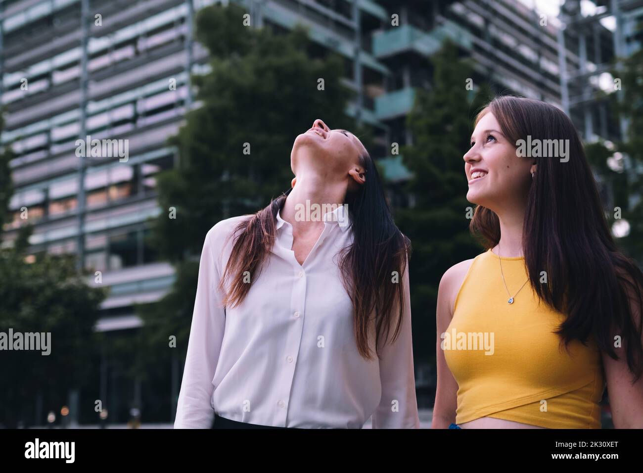 Woman with friend looking up in front of buildings Stock Photo - Alamy