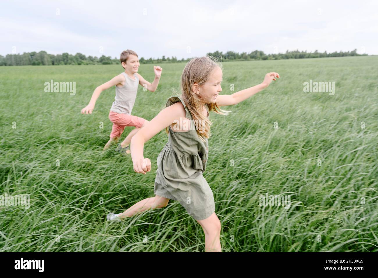 Happy siblings running on grass field Stock Photo - Alamy