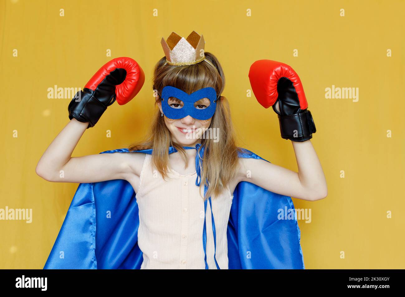 Girl in cape wearing mask and boxing gloves against yellow background ...