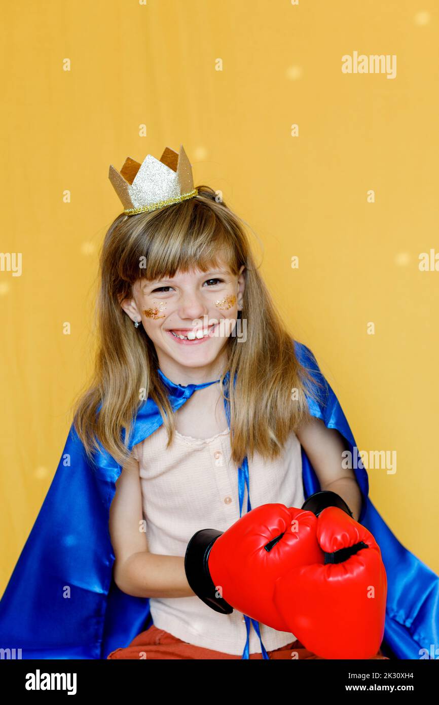 Cute girl wearing crown and boxing gloves against yellow background ...