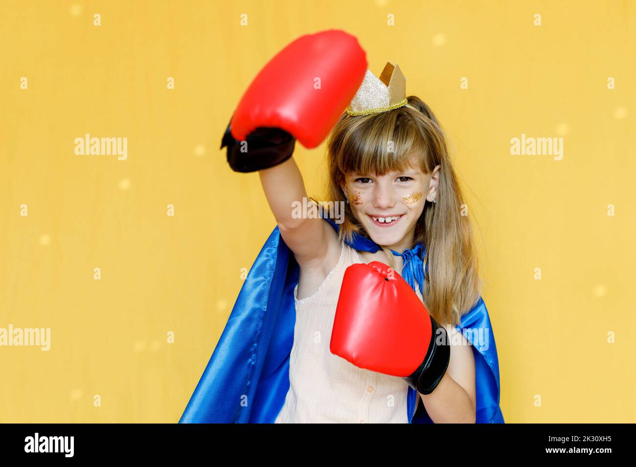 Happy girl wearing boxing gloves and cape against yellow background ...