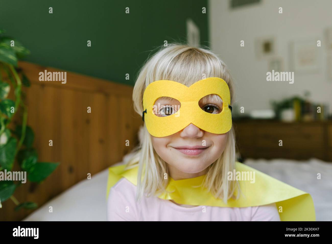 Smiling blond girl wearing yellow mask and cape at home Stock Photo - Alamy