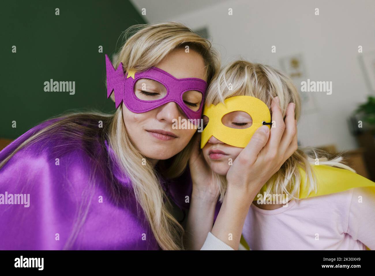 Mother and daughter with eyes closed wearing mask and cape at home ...