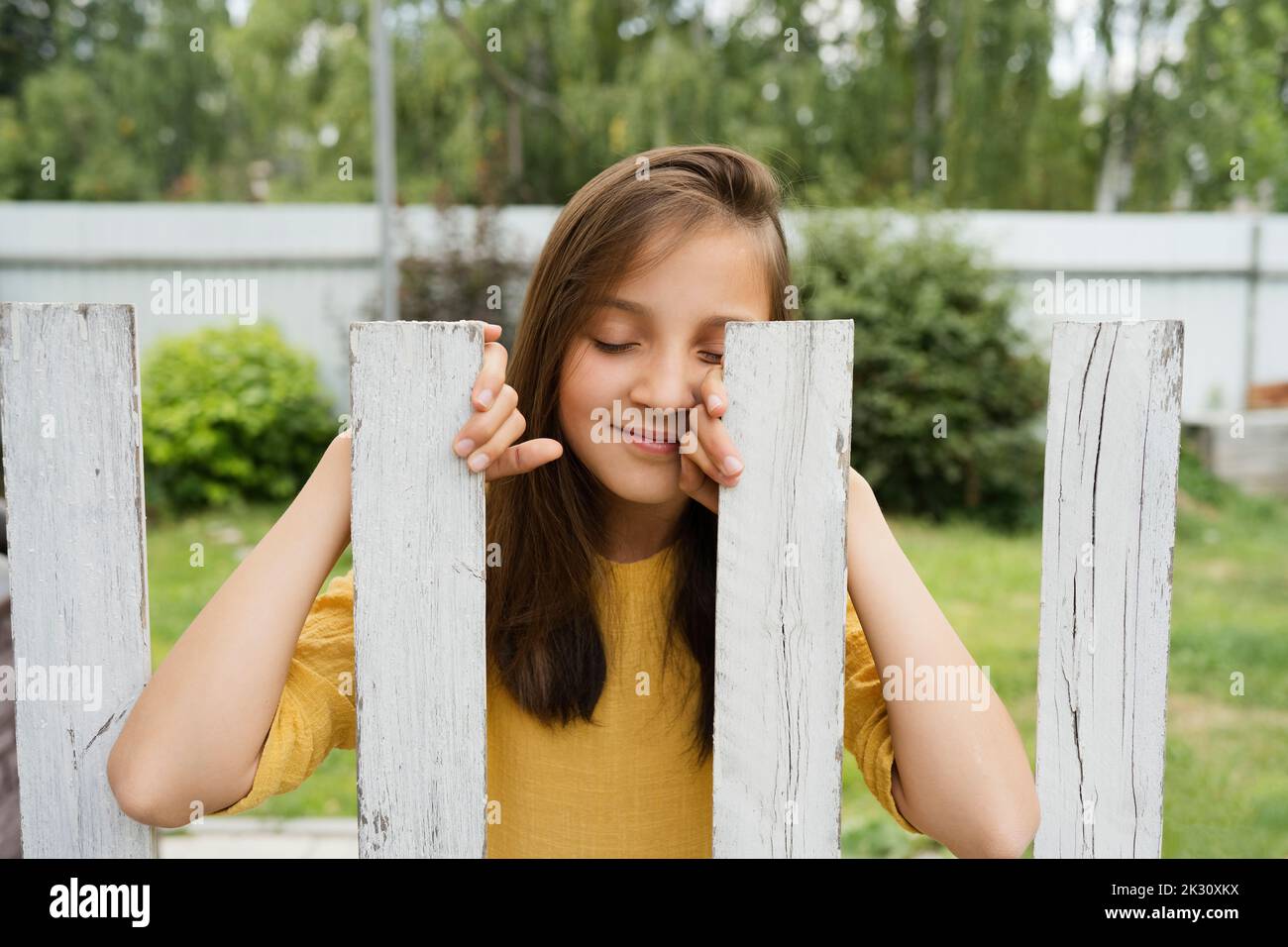 Smiling girl with eyes closed standing behind fence at back yard Stock ...