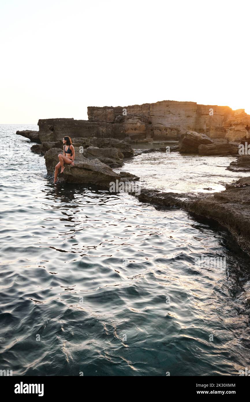 Woman relaxing on rock by sea Stock Photo - Alamy