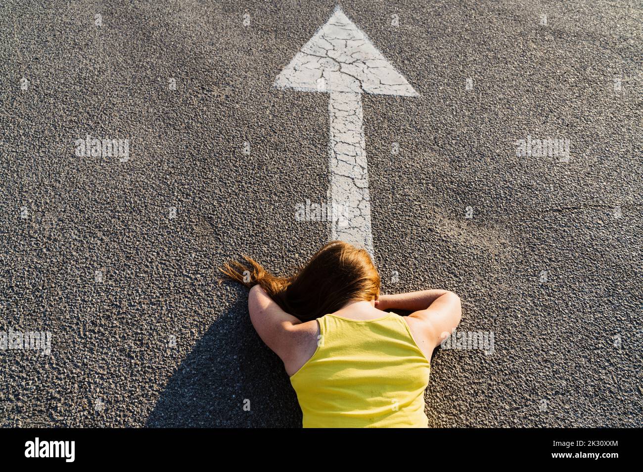 Woman lying with face down on arrow symbol over asphalt Stock Photo - Alamy