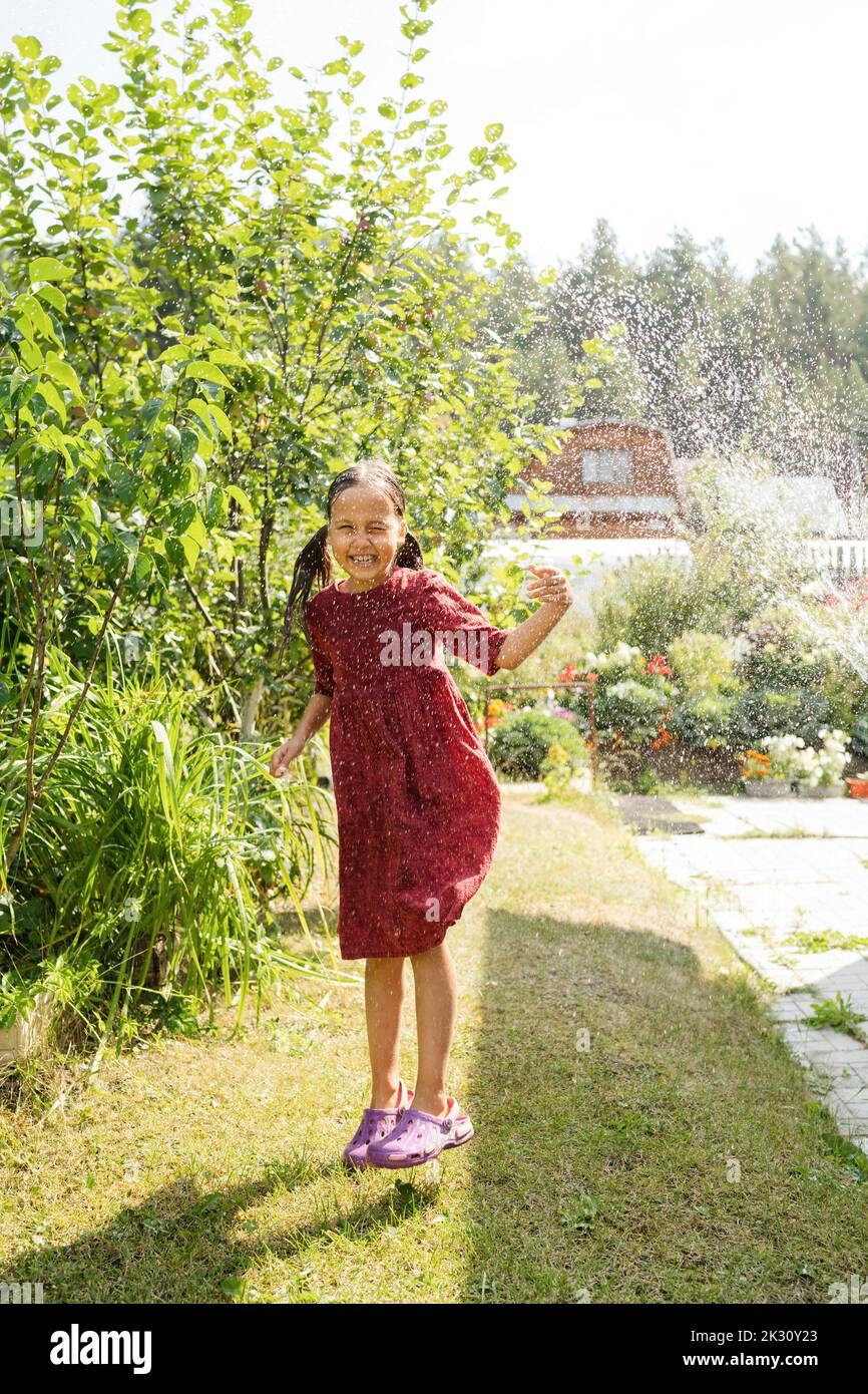 Cheerful girl jumping by splashing water in garden Stock Photo - Alamy