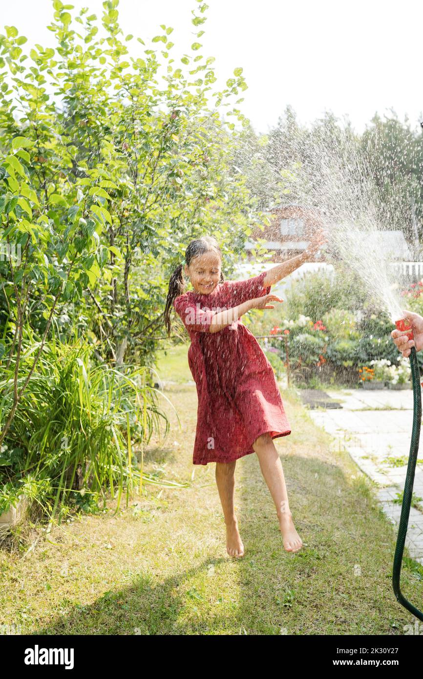 Carefree girl dancing in water from hose at garden Stock Photo - Alamy