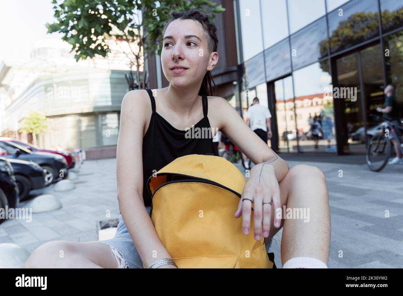 Contemplative non-binary person with backpack sitting on bench Stock ...