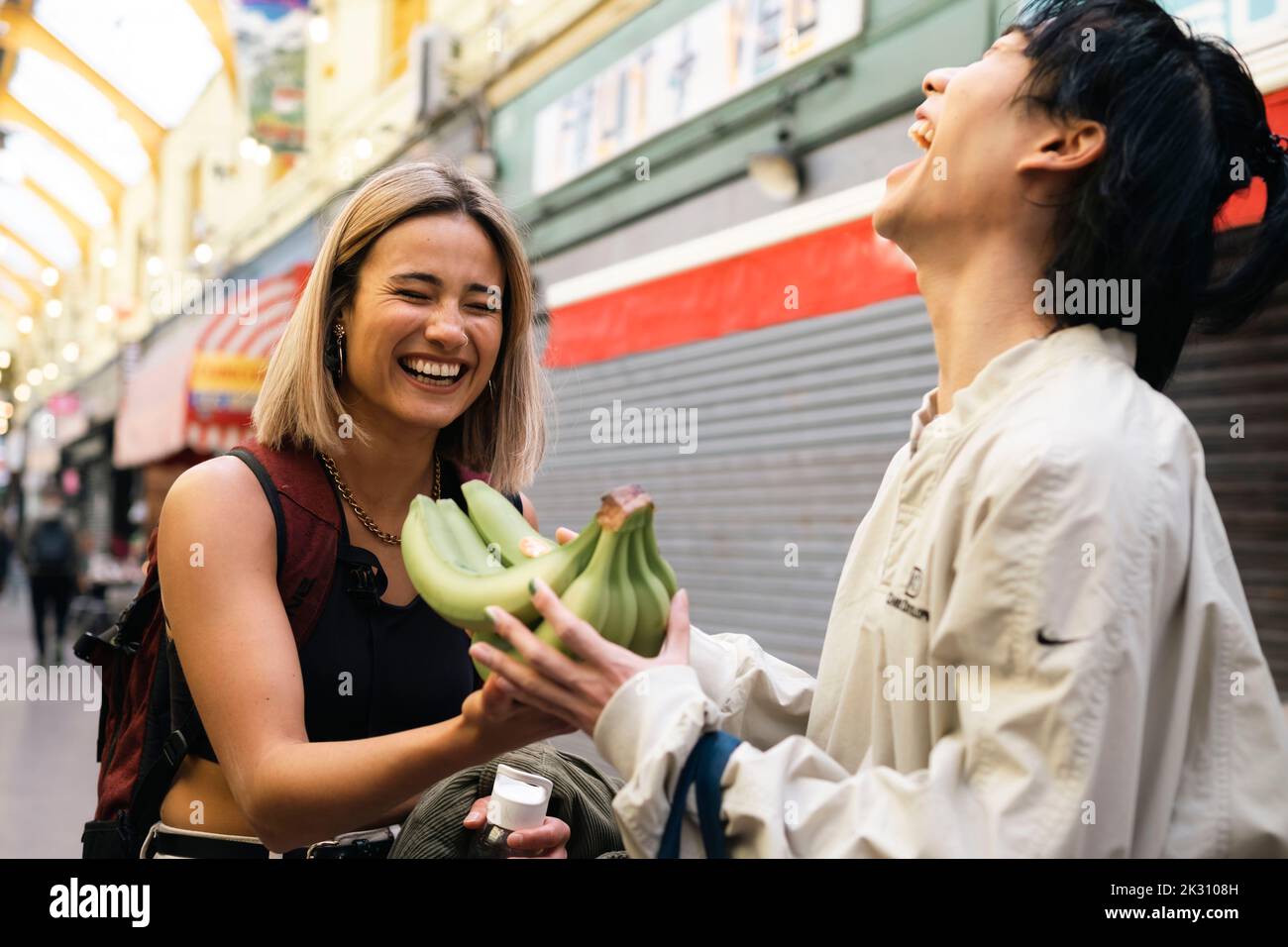 Happy young woman giving bananas to friend at street Stock Photo - Alamy