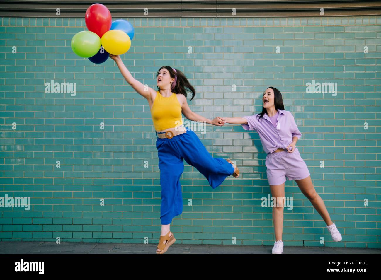 Woman catching friend holding multi colored balloons in front of ...