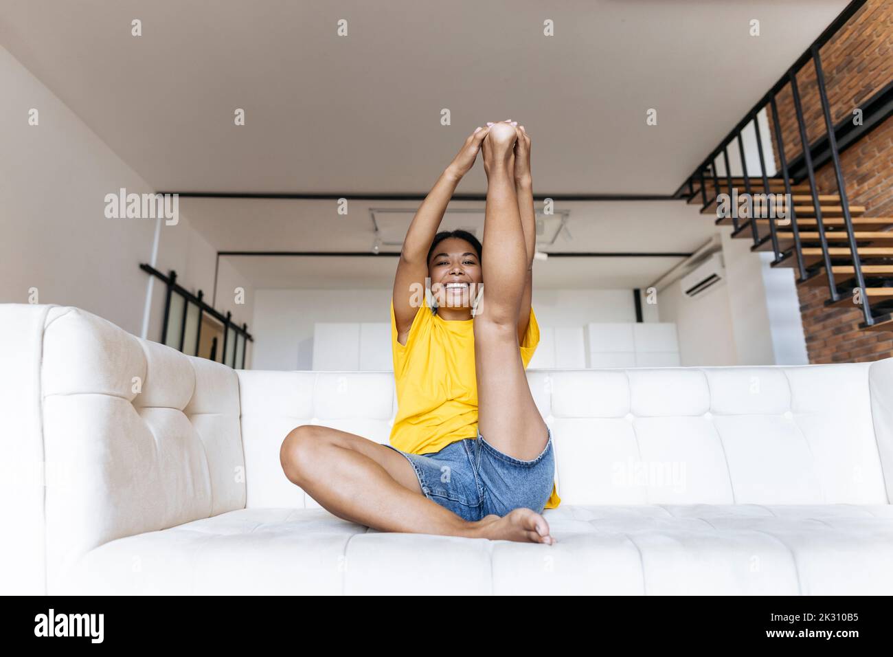 Cheerful woman sitting on sofa stretching her leg Stock Photo - Alamy