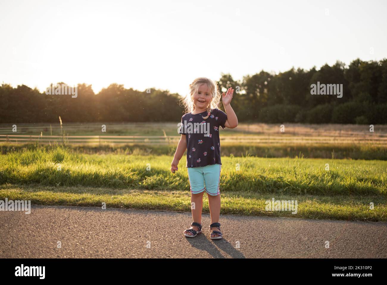Happy cute girl waving standing on sunny day Stock Photo - Alamy