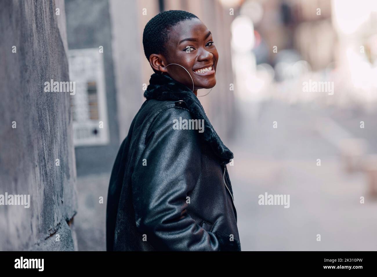Happy woman wearing leather jacket by wall Stock Photo - Alamy