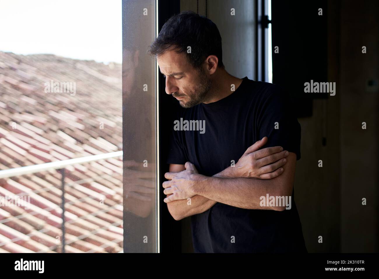 Depressed man with arms crossed standing by window Stock Photo - Alamy