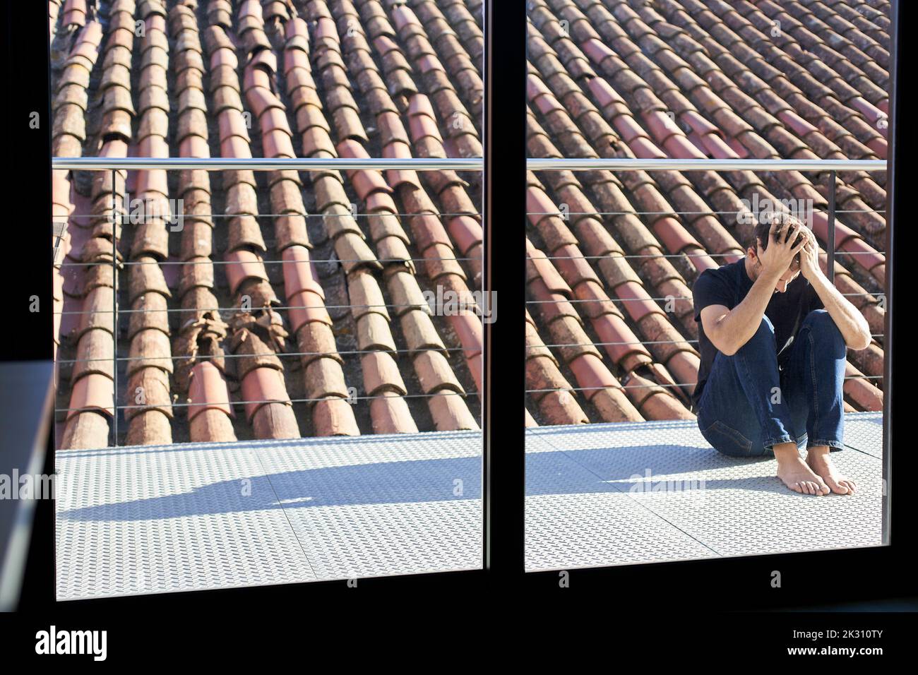 Man sitting with head in hands at balcony seen through window Stock ...