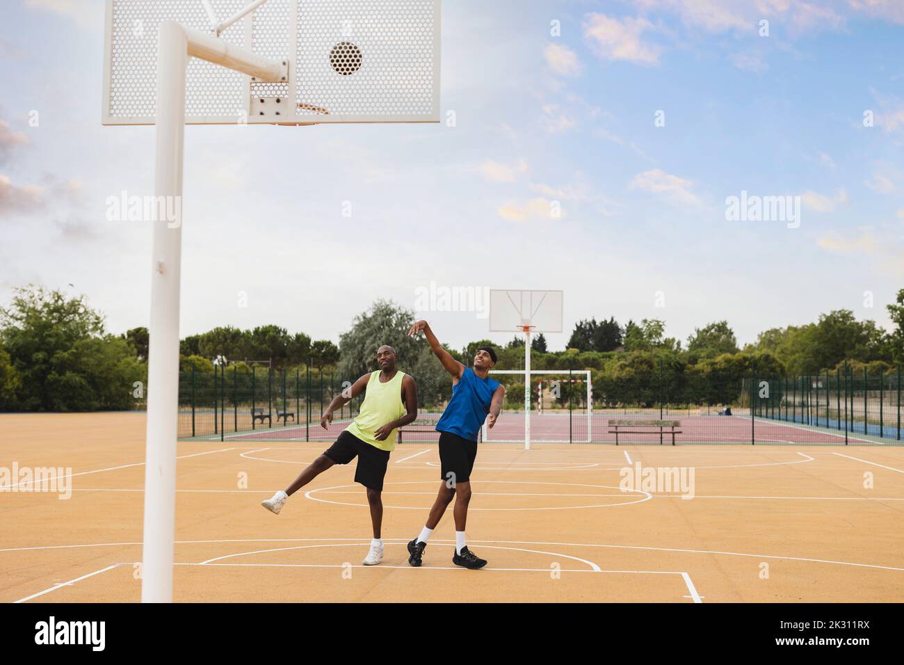 Young man throwing basketball in hoop playing with father at sports ...
