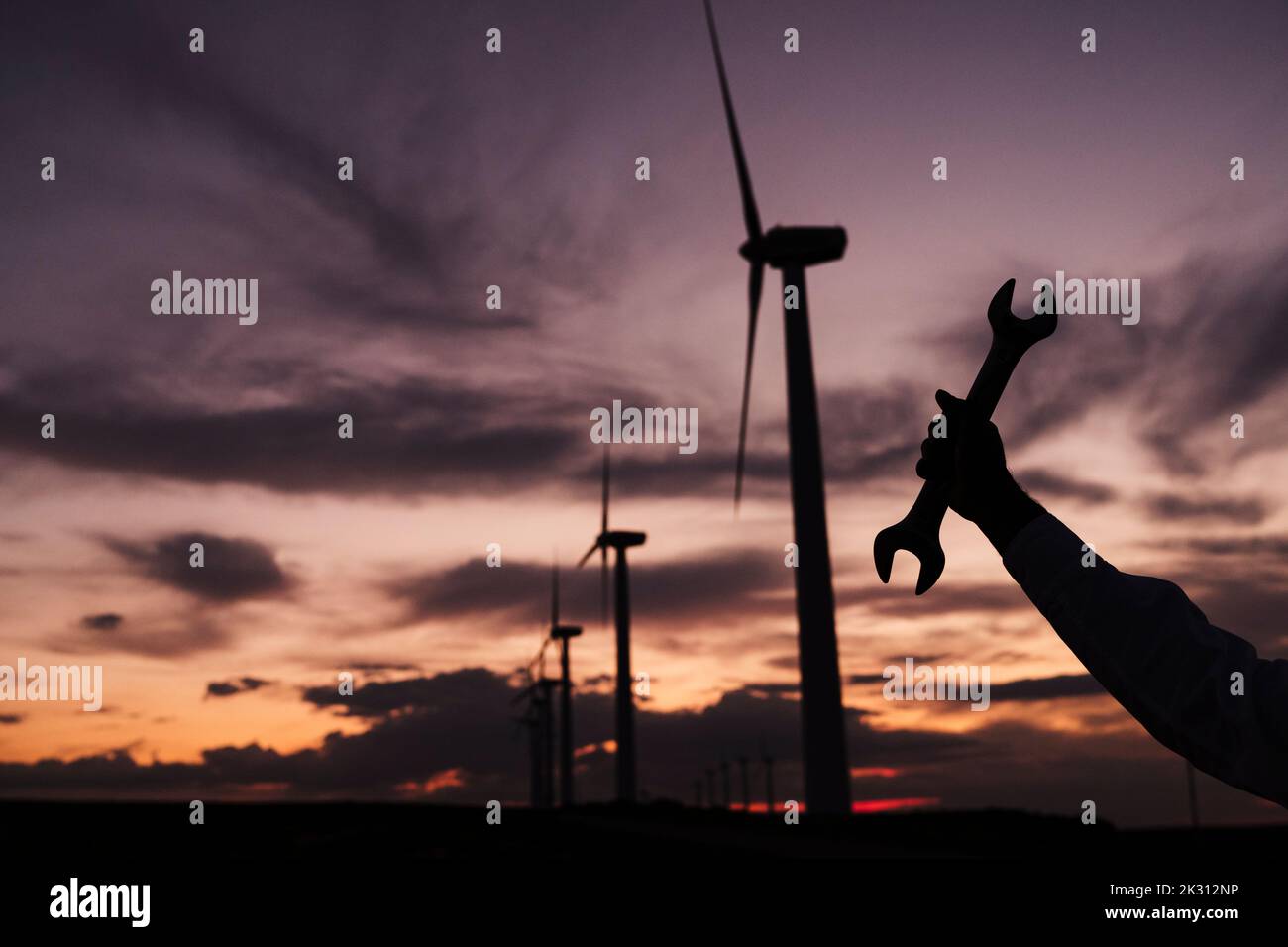 Silhouette of engineer holding wrench by wind turbines at wind farm on ...