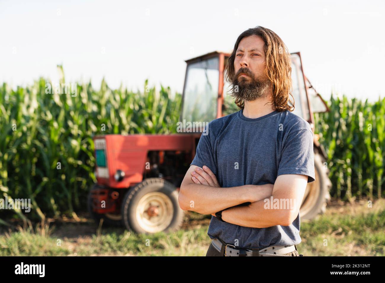 Contemplative bearded farmer with arms crossed standing in front of ...