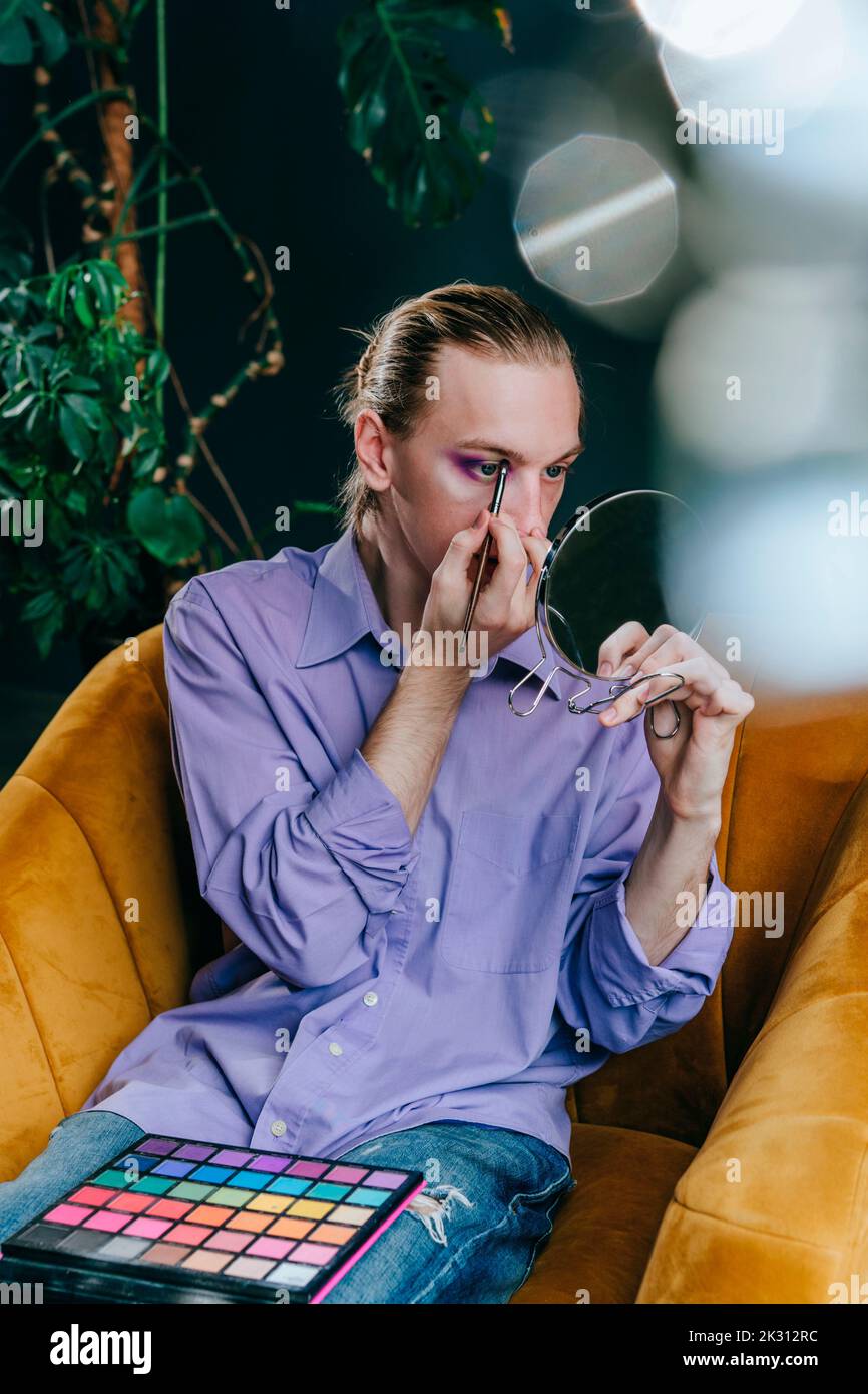 Man applying eyeshadow sitting on chair Stock Photo - Alamy