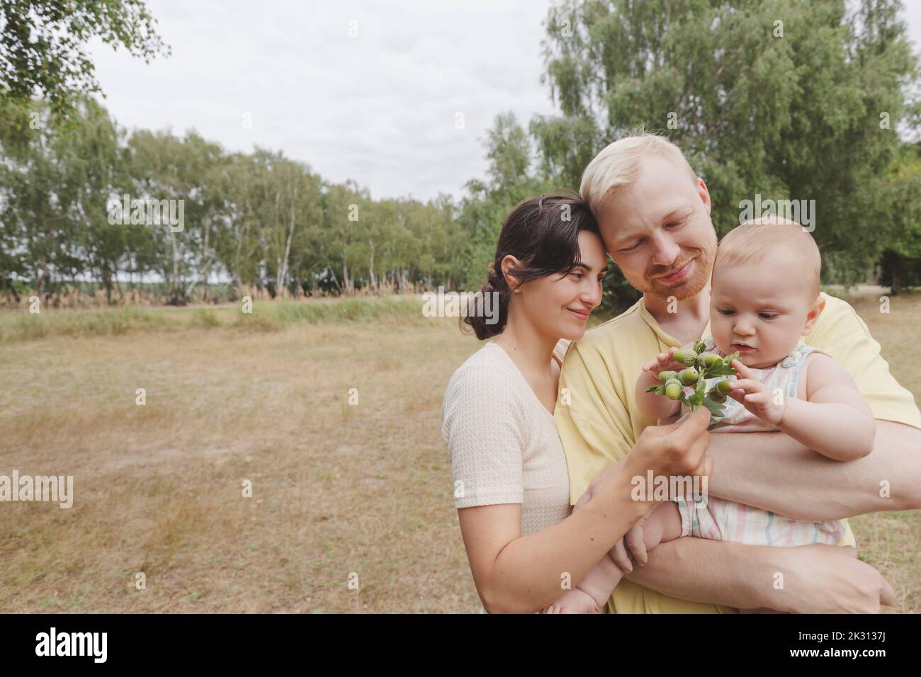 Baby girl playing with oak branch by parents in park Stock Photo - Alamy