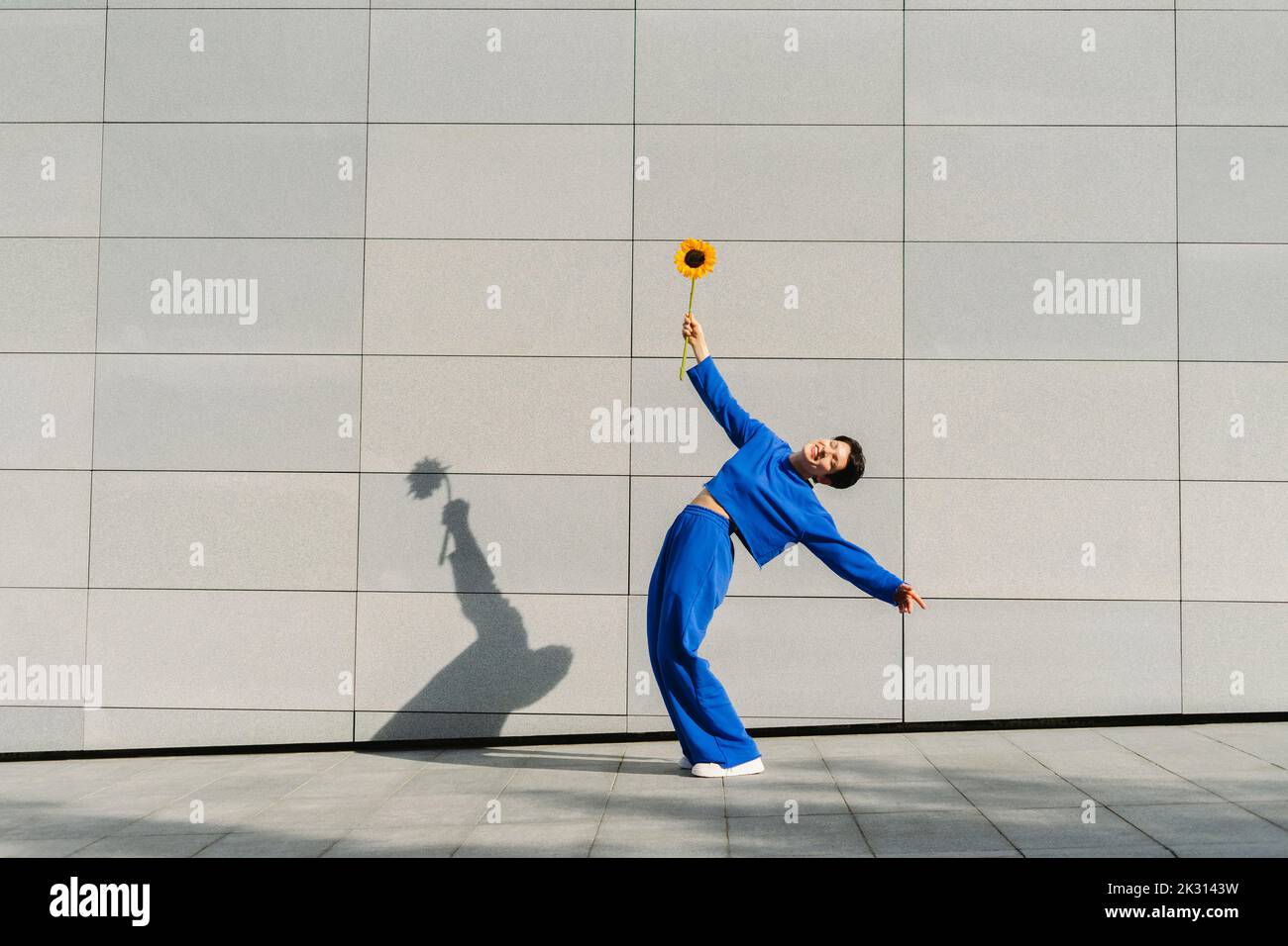 Happy woman with sunflower bending over backwards by wall Stock Photo ...
