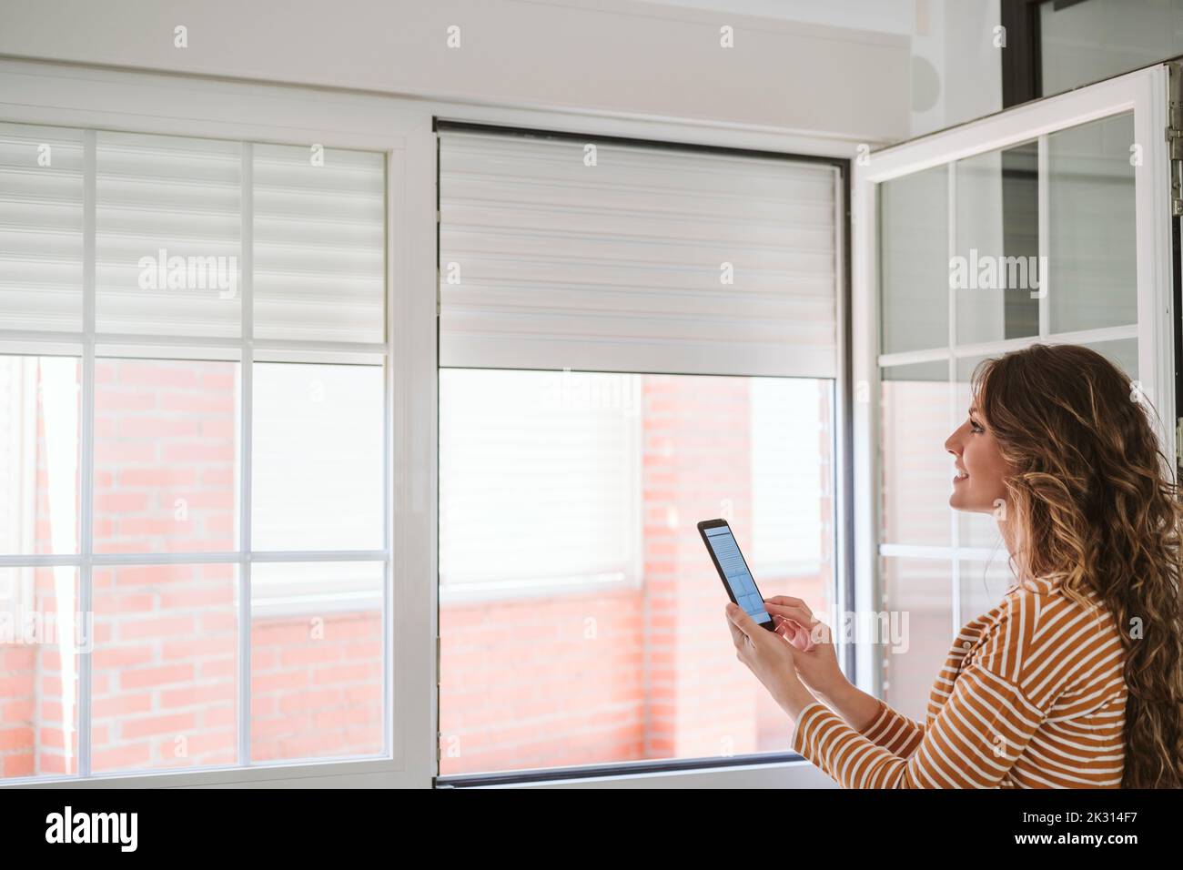 Young woman at home using mobile phone app to control blinds Stock ...