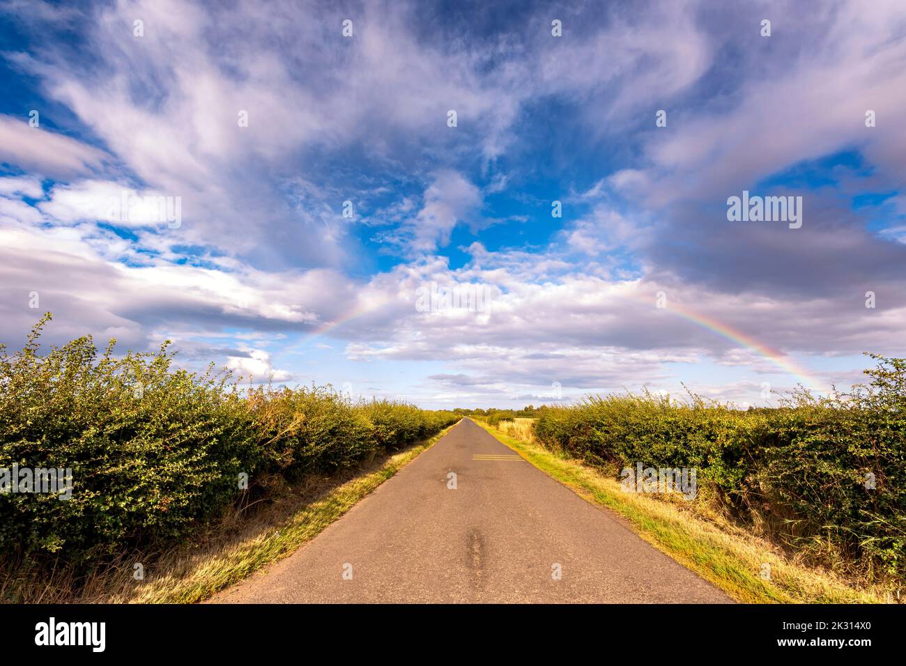 UK, Scotland, Rainbow arching against clouds floating over country road ...