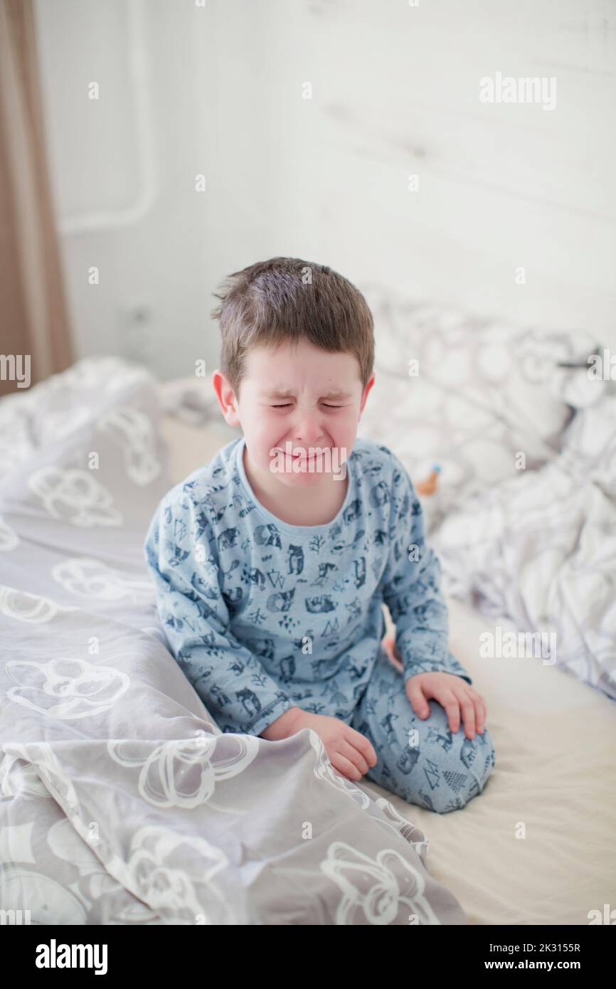 Crying boy sitting on bed at home Stock Photo - Alamy