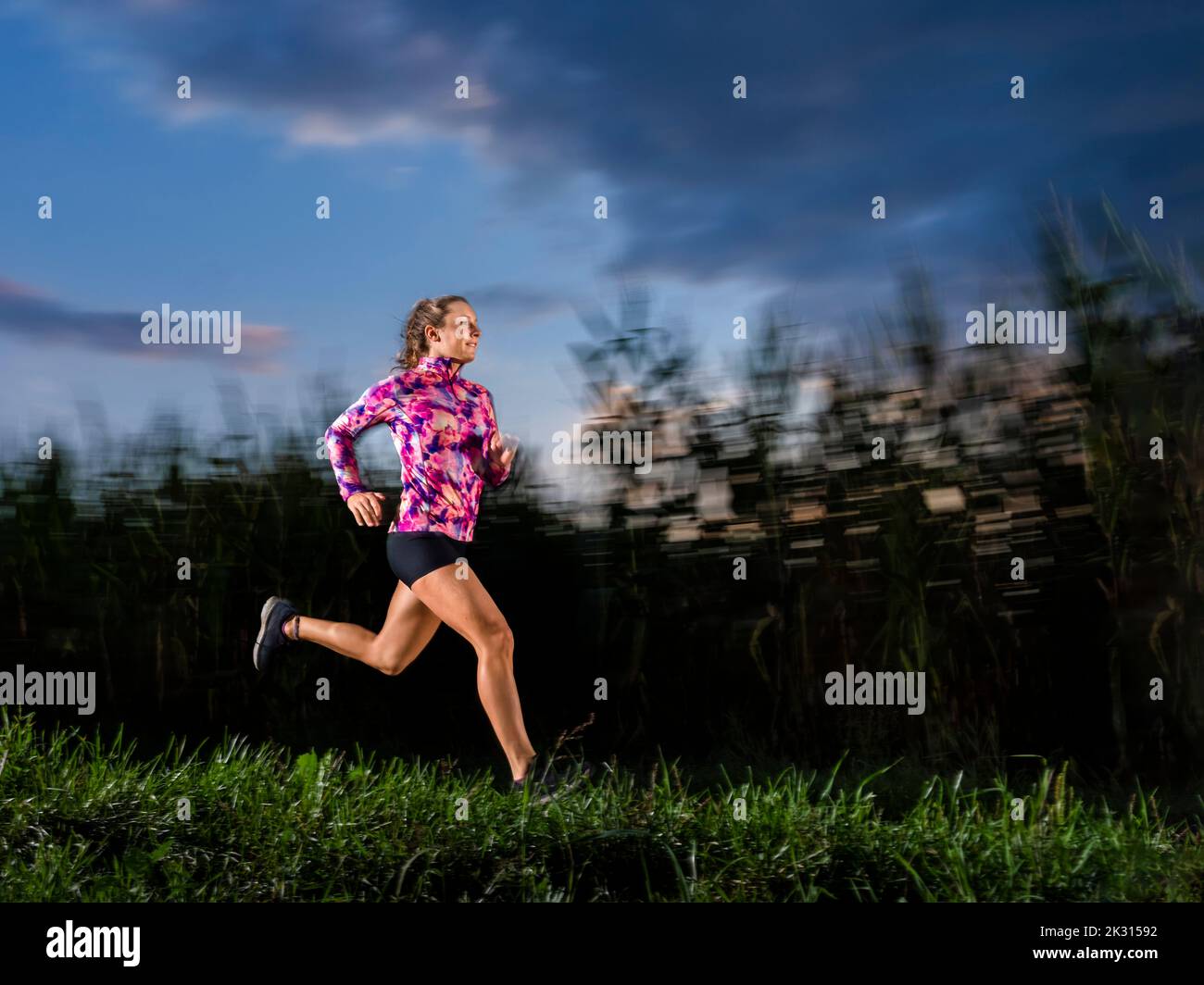 Young sportswoman running on grass at dusk Stock Photo - Alamy