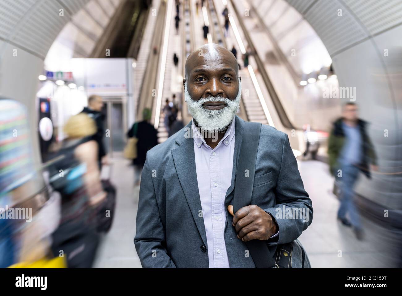 Smiling bald businessman with laptop bag amidst commuters at subway ...
