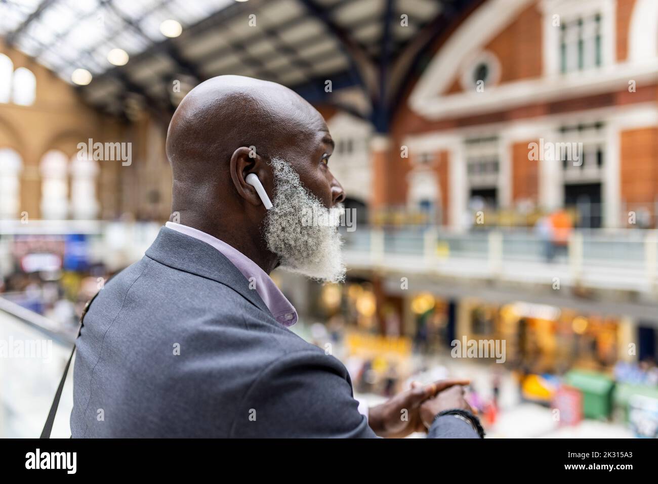 Bald senior commuter listening to music through wireless in-ear ...