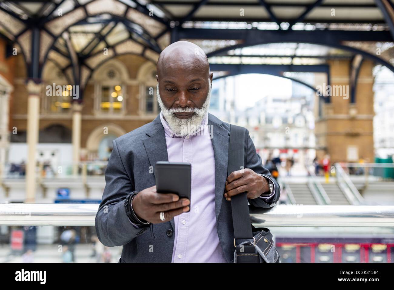 Senior commuter using mobile phone at railroad station Stock Photo - Alamy
