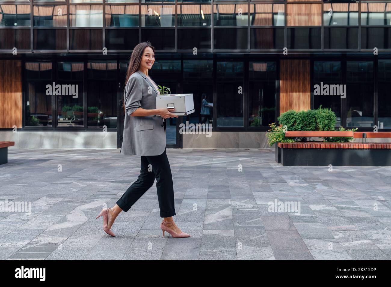 Smiling businesswoman walking with box in front of office building ...