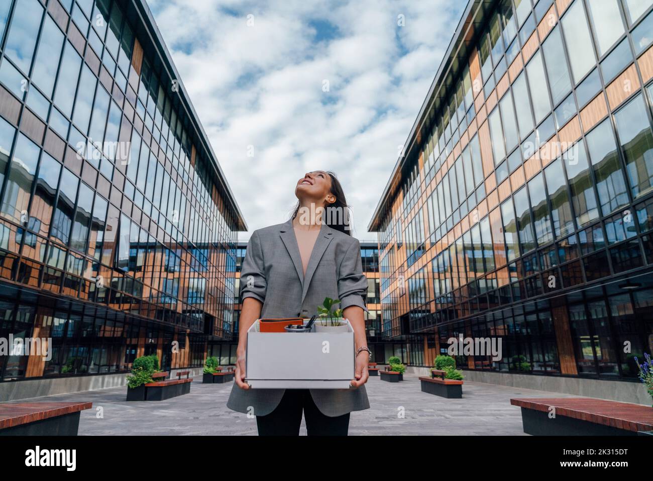 Smiling businesswoman carrying box in front of office building under ...