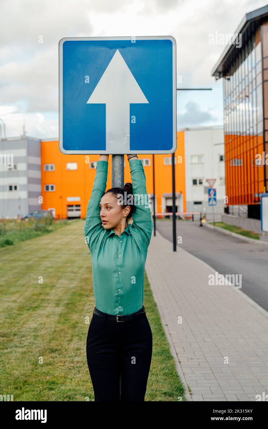 Businesswoman with arms raised holding arrow sign board on footpath ...
