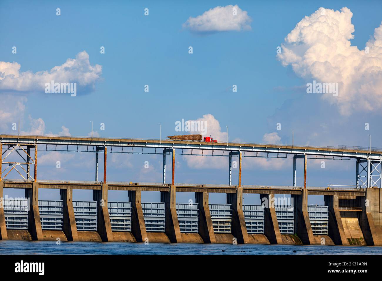 Red logging truck driving over Pickwick lock and dam on a bright sunny ...