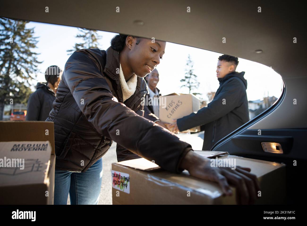 Young woman unloading donation boxes from car in parking lot Stock ...