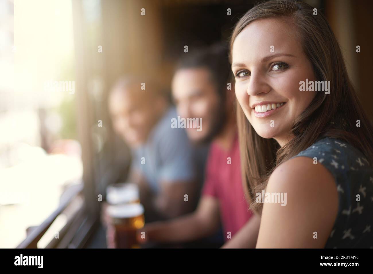 Pull up a chair. Portrait of a smiling young woman in a bar with some ...