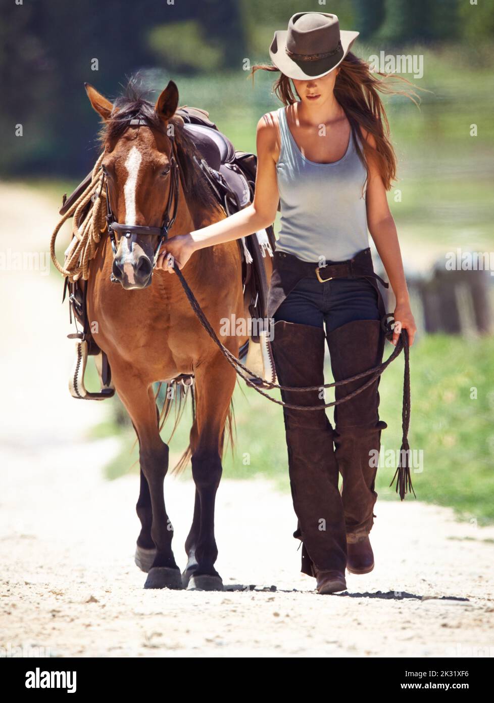 Loving the outdoors. A gorgeous cowgirl leading her horse along a country lane Stock Photo - Alamy