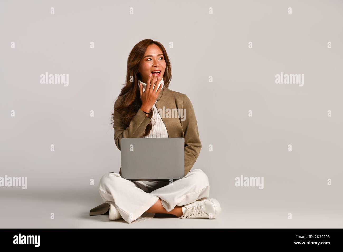 Excited woman sitting with laptop and looking at copy space over white ...
