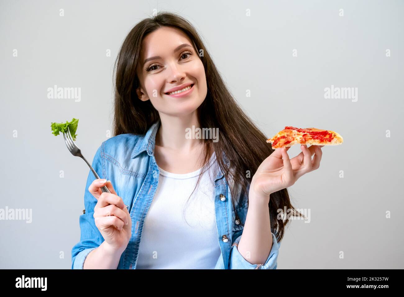Young smiling woman chooses what to eat, pizza or salad Stock Photo - Alamy