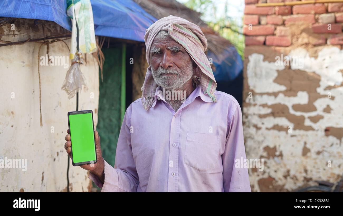 Indian old man holding a mobile phone and point towards it's screen ...