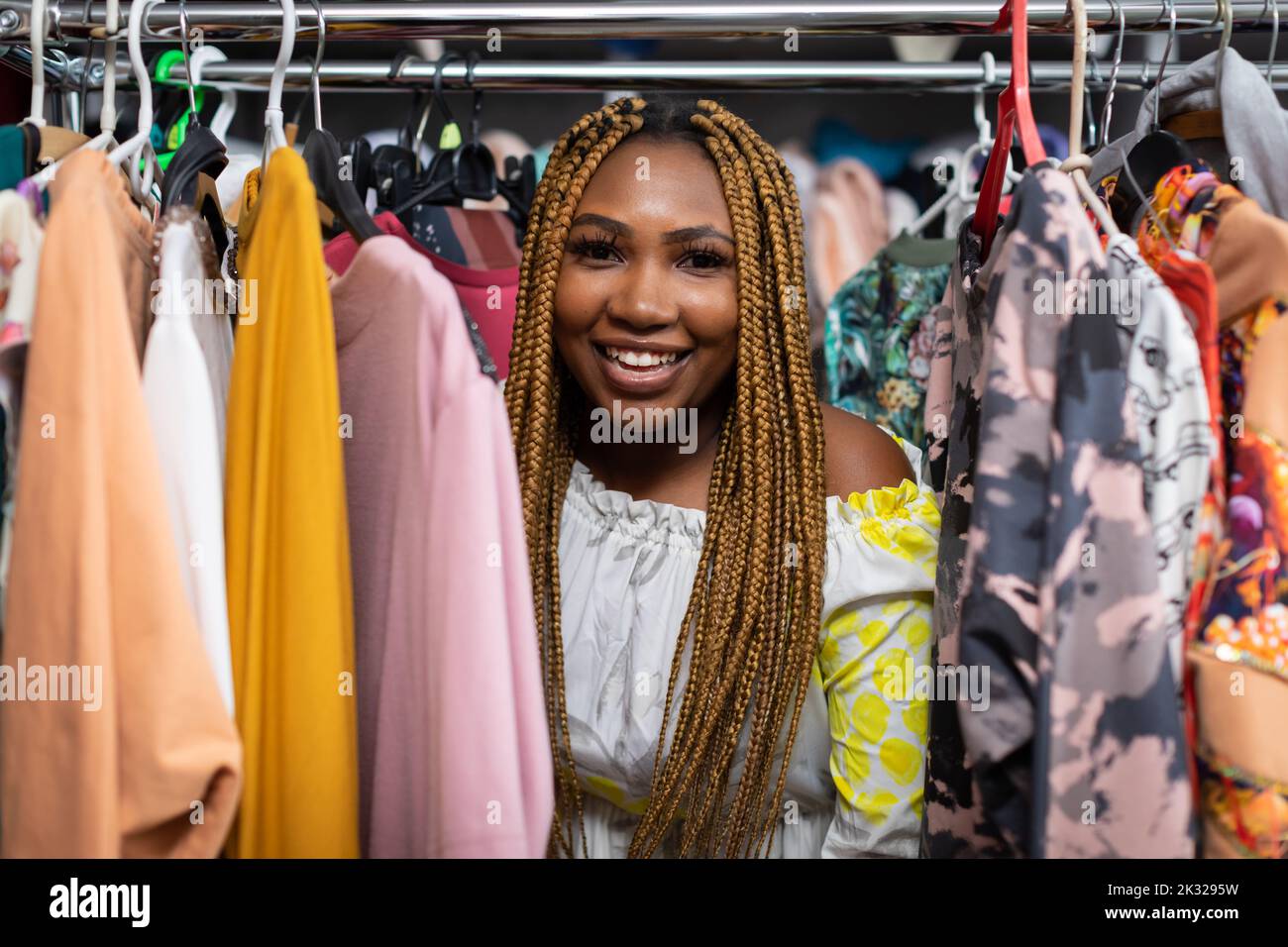 A Smiling Dark Skinned Woman Leans Out From Behind A Rack Full Of