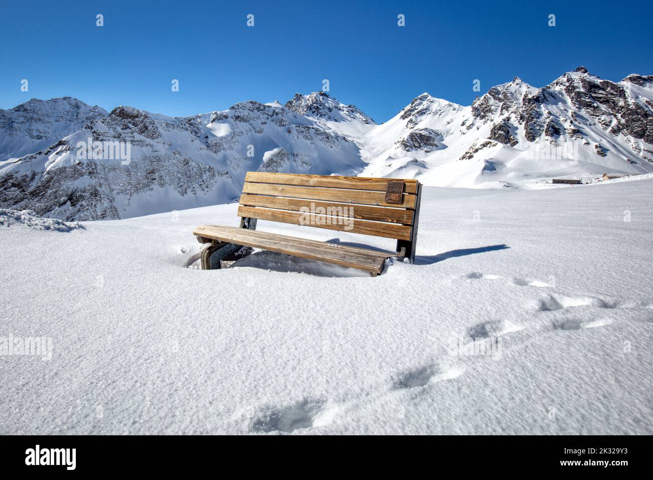 Wooden bench in the snow-capped Swiss Alps under a blue sky, winter ...