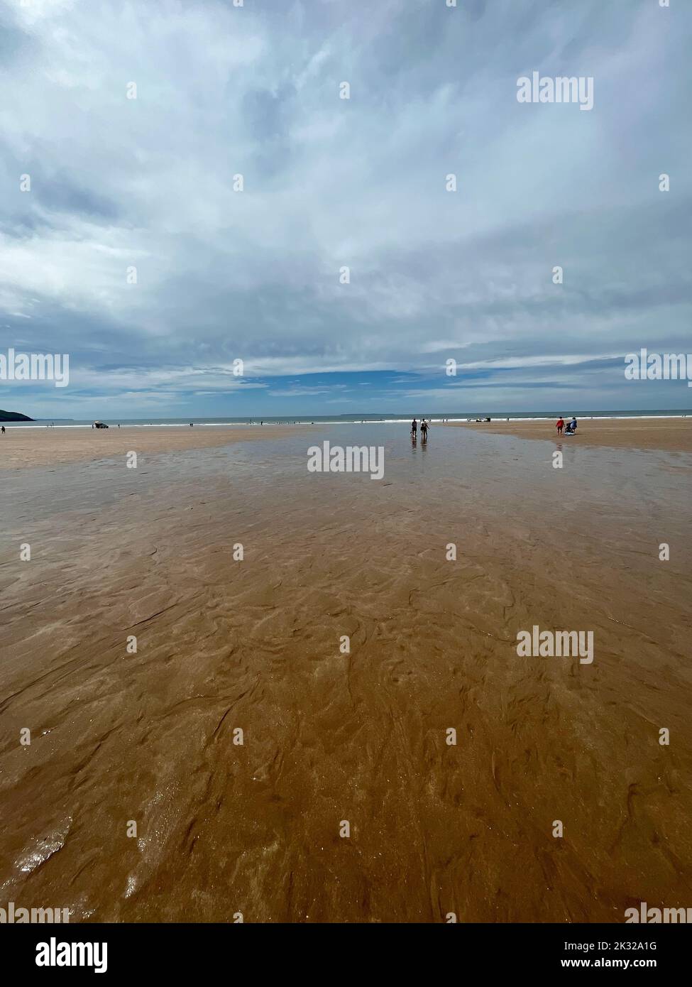 A vertical shot of a calm shallow coast with people walking on the ...