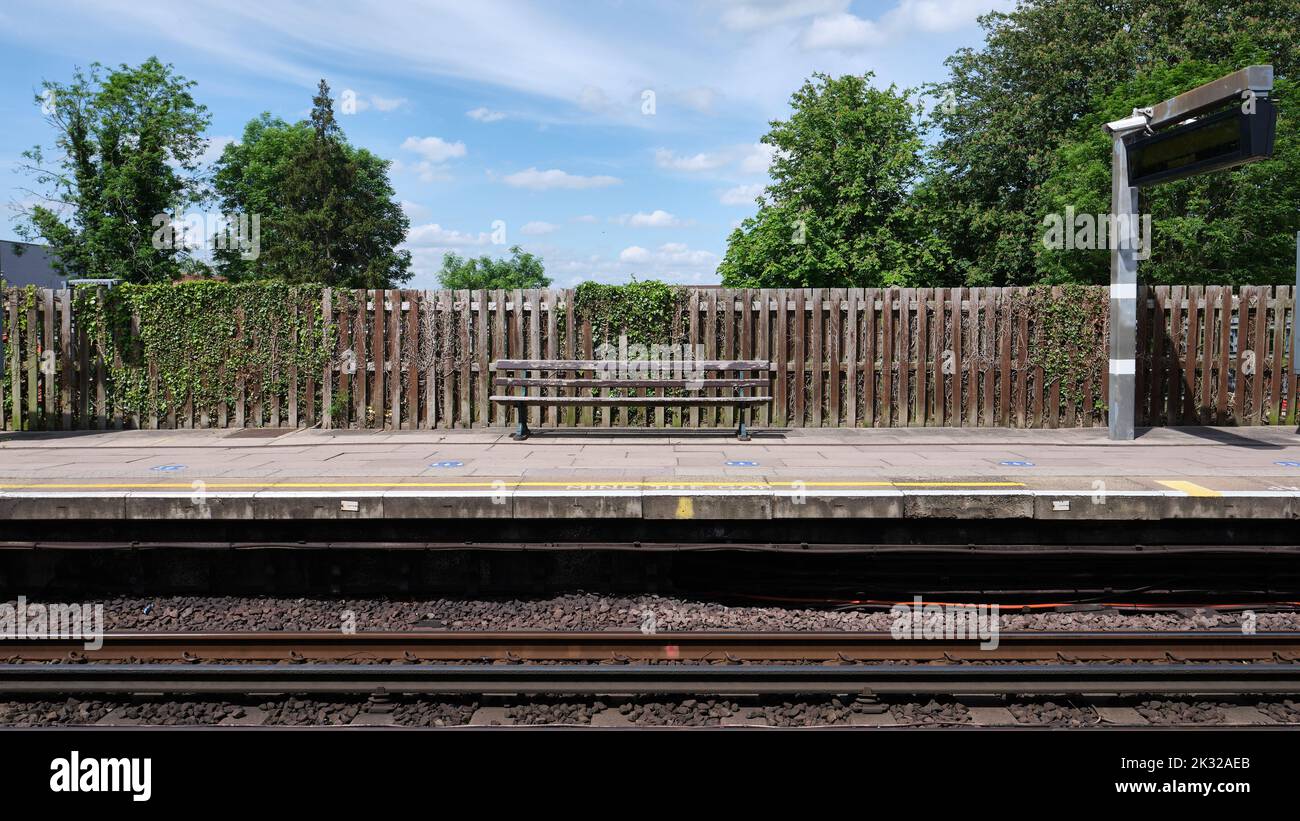 Train station platform with a wooden bench and fence. Trees and blue ...