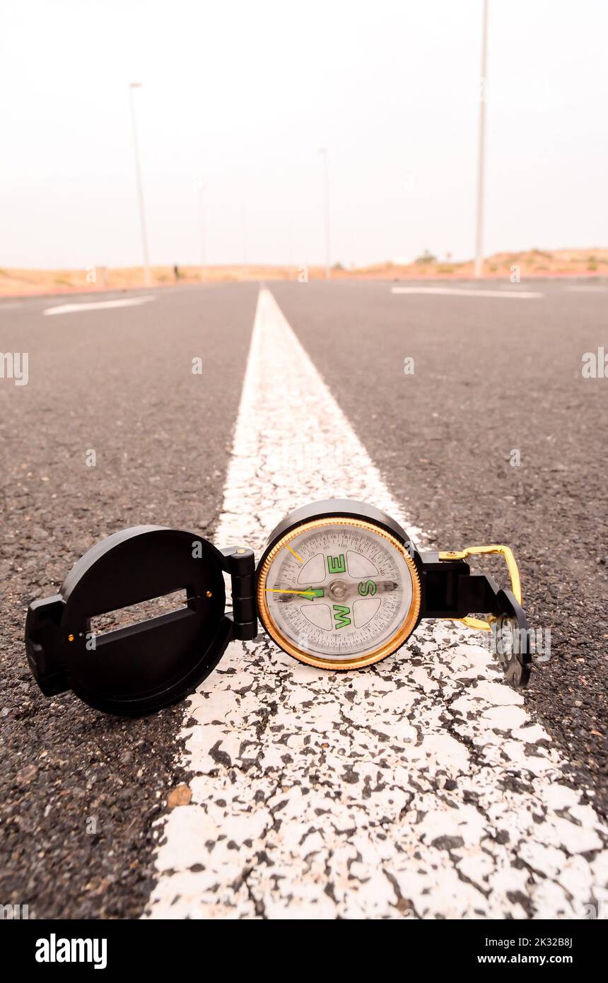 A vertical closeup of a compass on an asphalt road - travel concept ...