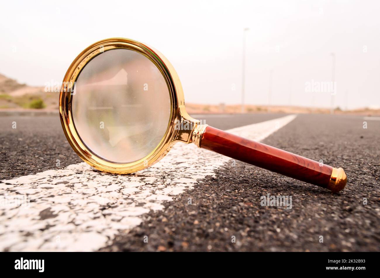 A closeup of a magnifying glass on an asphalt road - travel concept ...