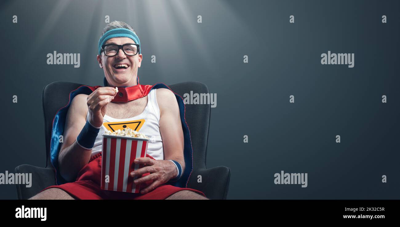 Funny happy superhero watching comedy movies and eating popcorn, he is ...